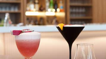 Um bar com um coquetel em taça, uma taça martini e um copo de whisky sobre jogos americanos.