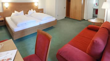 Quarto de hotel com uma cama, um sofá vermelho, um guarda-roupa de madeira e uma pequena mesa com abajur.