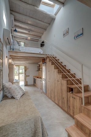 Um quarto amplo com uma cama grande, escada de madeira e uma área de cozinha.