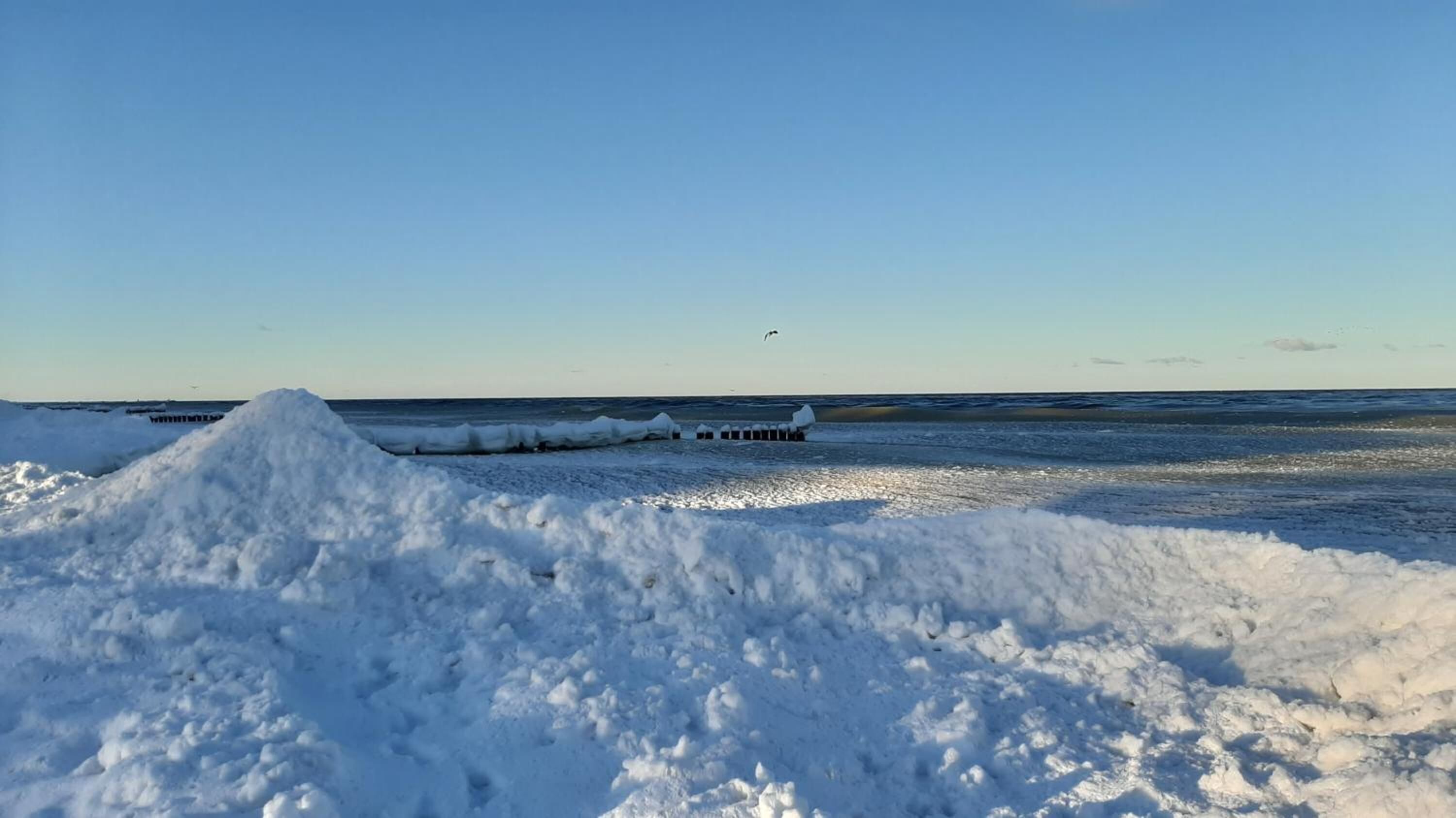 Uma praia coberta de neve, com um monte de neve em primeiro plano e céu limpo.