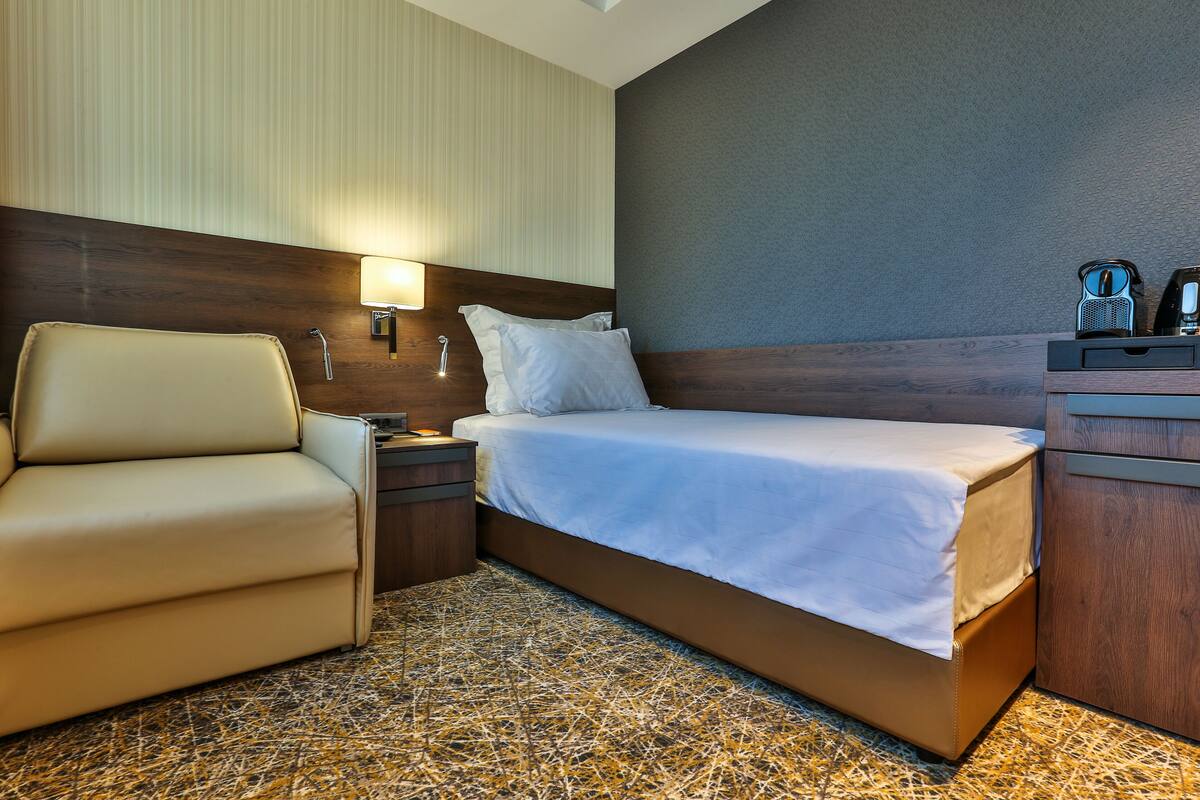 Quarto de hotel com cama, cadeira, mesa de cabeceira e abajur.