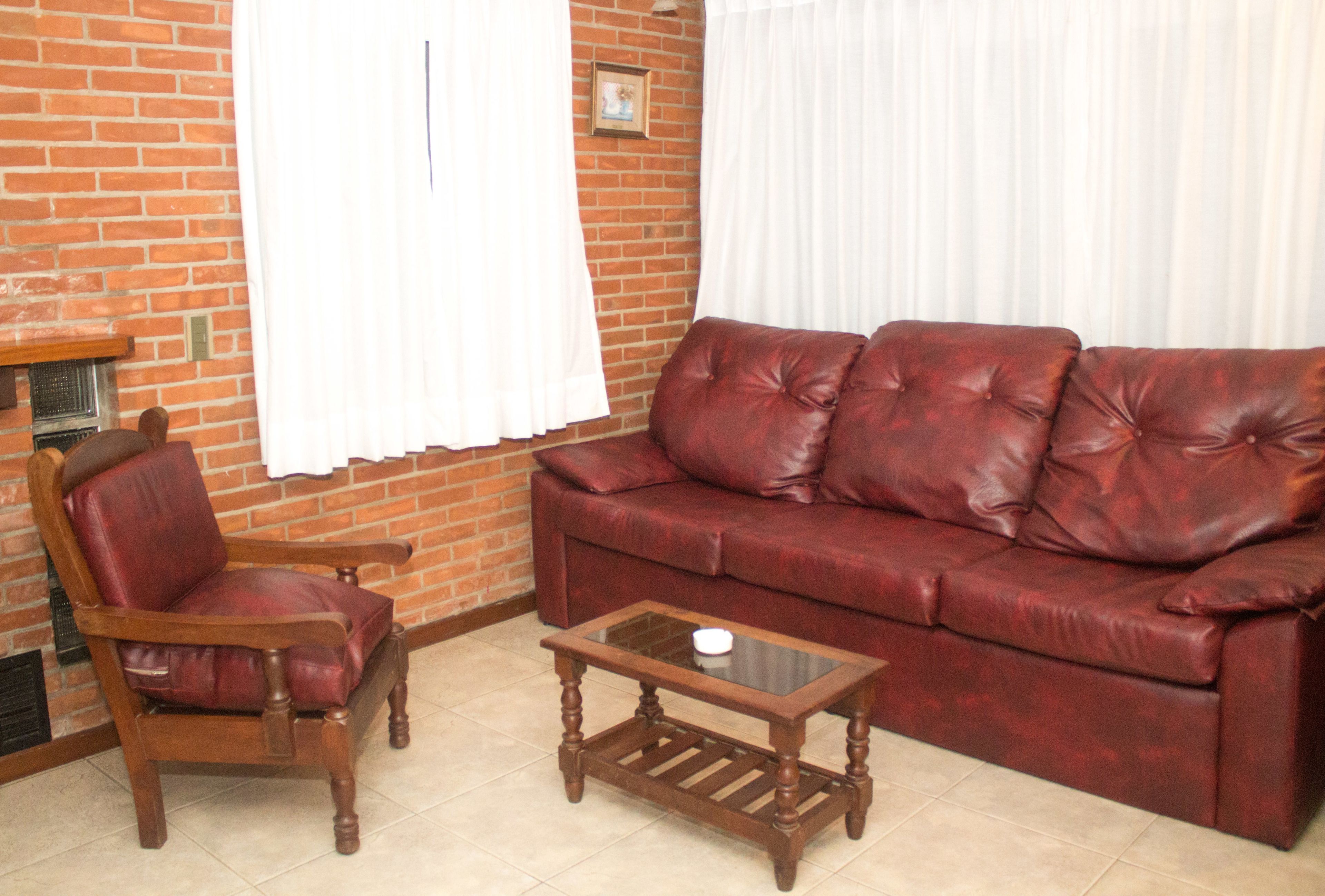 Uma sala de estar com um sofá de couro vermelho, uma cadeira de madeira e uma mesa de centro com tampo de vidro.