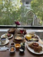 Mesa de pequeno-almoço com diversos alimentos e vista para um edifício com arco gótico.