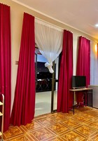 Quarto com cortinas vermelhas, uma televisão sobre suporte e um chão estampado.