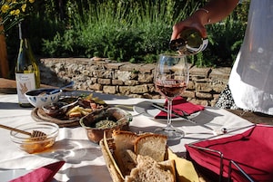 Mesa posta ao ar livre com uma garrafa de vinho, um copo de vinho, pão e um recipiente com mel.