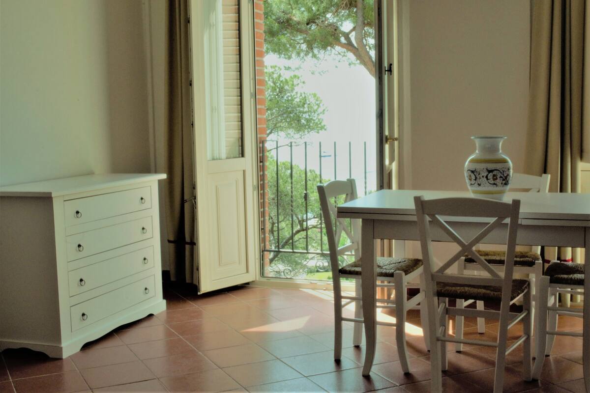 Uma sala de jantar com mesa, cadeiras, um vaso e um armário branco.