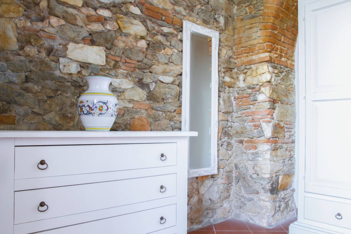 Pared de pedra com um armário branco e um vaso.