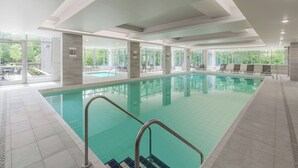Uma grande piscina interna com vista clara para o exterior, rodeada por áreas de estar e arquitetura moderna.