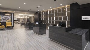 Uma área de recepção de hotel moderna com piso de mármore, lareira e uma placa com a inscrição "MARRIOTT BONVOY".
