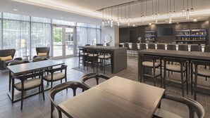 Um saguão moderno de hotel com área de bar, assentos e uma grande janela que oferece luz natural.
