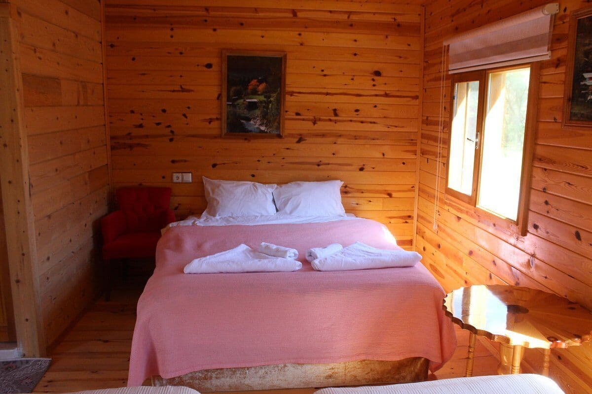 Quarto de cabana de madeira com uma cama, uma cadeira vermelha e uma mesa pequena.