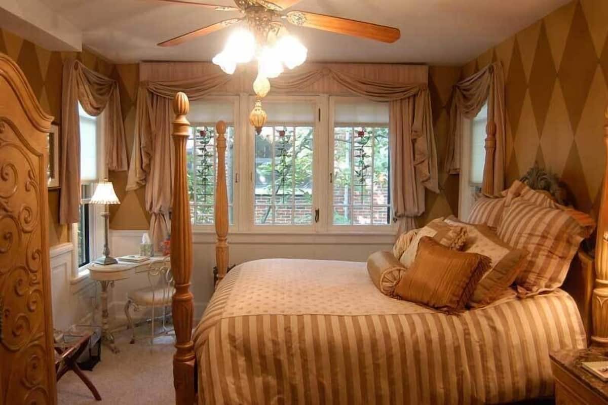 Quarto com cama grande, cabeceira de madeira, ventoinha de teto e janela com cortinas.