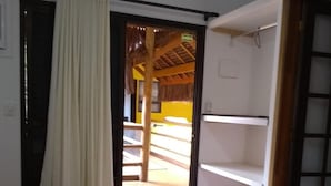 Quarto com cama, cortina, porta para área externa e estante.