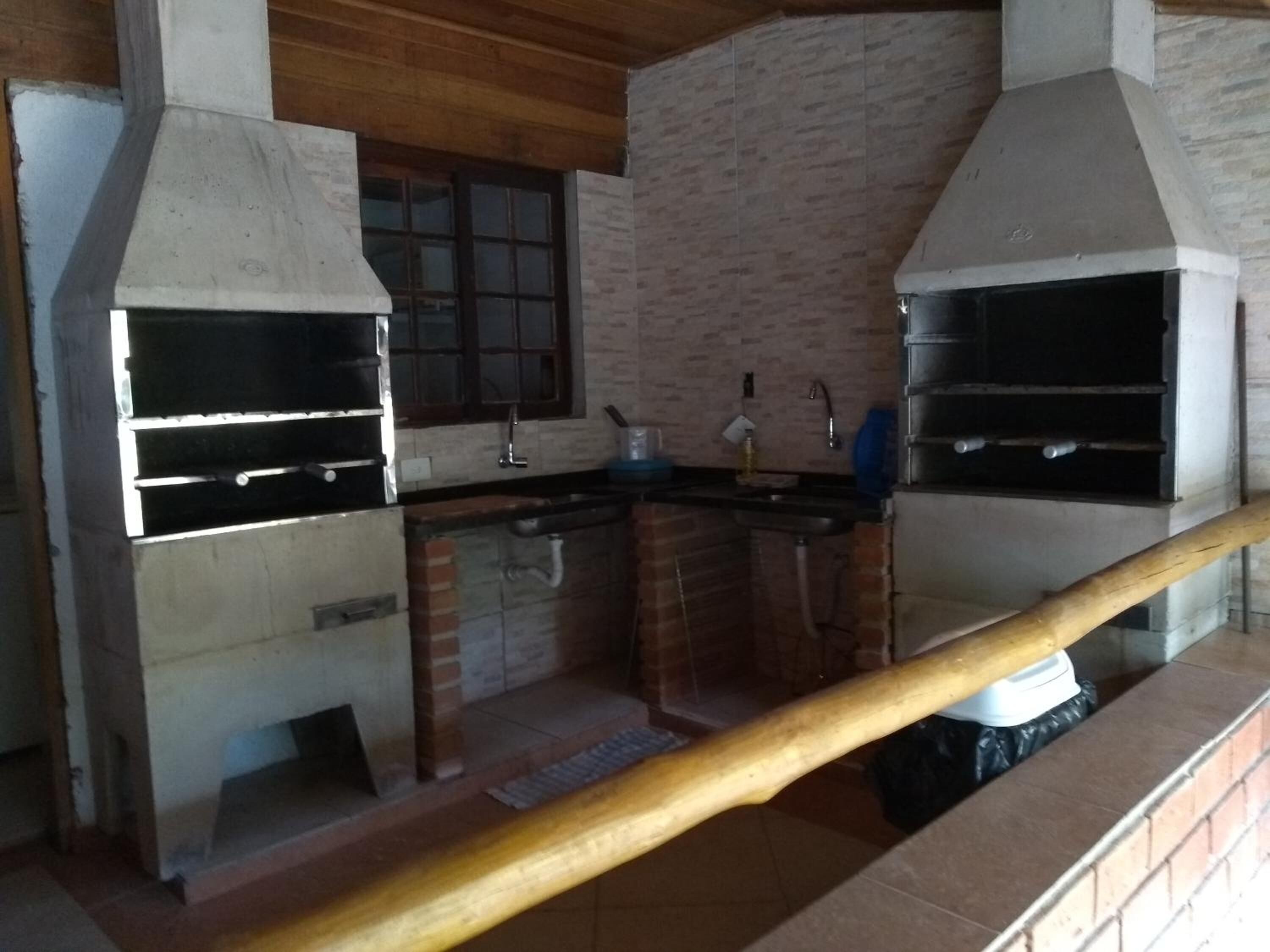 Uma cozinha com duas fornalhas a lenha embutidas, painel de fundo de tijolos e uma janela.