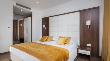 Quarto de hotel com uma cama grande, cabeceira de madeira, mesa de cabeceira e luminária fixa na parede.