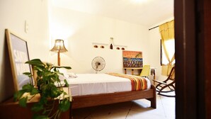Quarto com cama, luminária de cabeceira, ventilador e um quadro na parede.