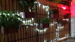 Cercado de madeira com ripas verticais, decorado com luzes de cordão e vasos de plantas.