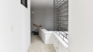Um corredor estreito com uma banheira branca, piso ladrilhado e corrimão de metal.