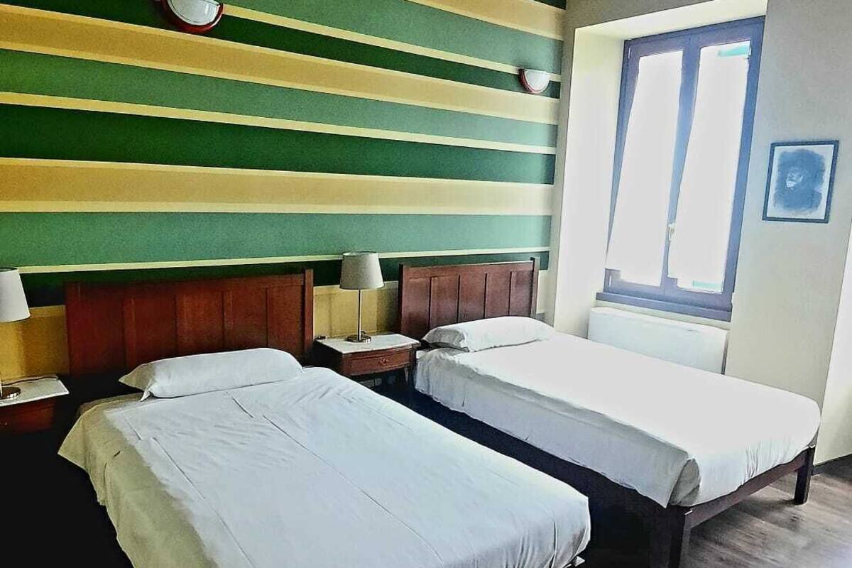 Quarto com duas camas, vigas de madeira no teto e parede listrada.