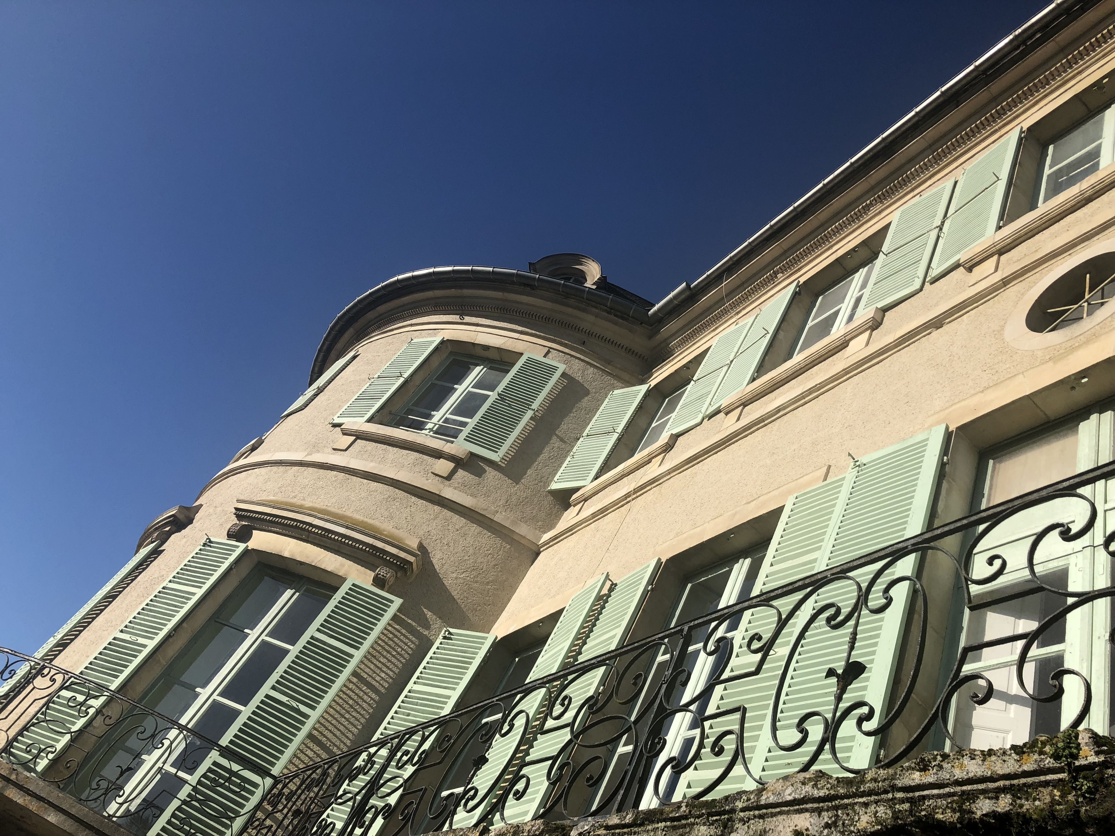 Um edifício histórico com fachada curva, persianas verdes e grades de ferro ornamentadas.
