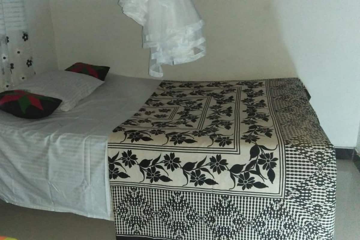 Uma cama de solteiro com colcha estampada de flores, um travesseiro branco e um travesseiro decorativo com padrão vermelho e verde.