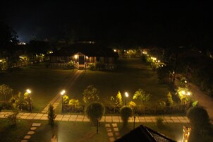 Vista noturna de um resort com caminhos iluminados, um edifício central e vegetação ao redor.
