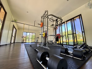 Uma academia espaçosa com amplas janelas, diversos equipamentos de musculação e piso de madeira.