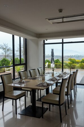 Uma sala de jantar com uma mesa comprida, cadeiras e vista para o exterior.