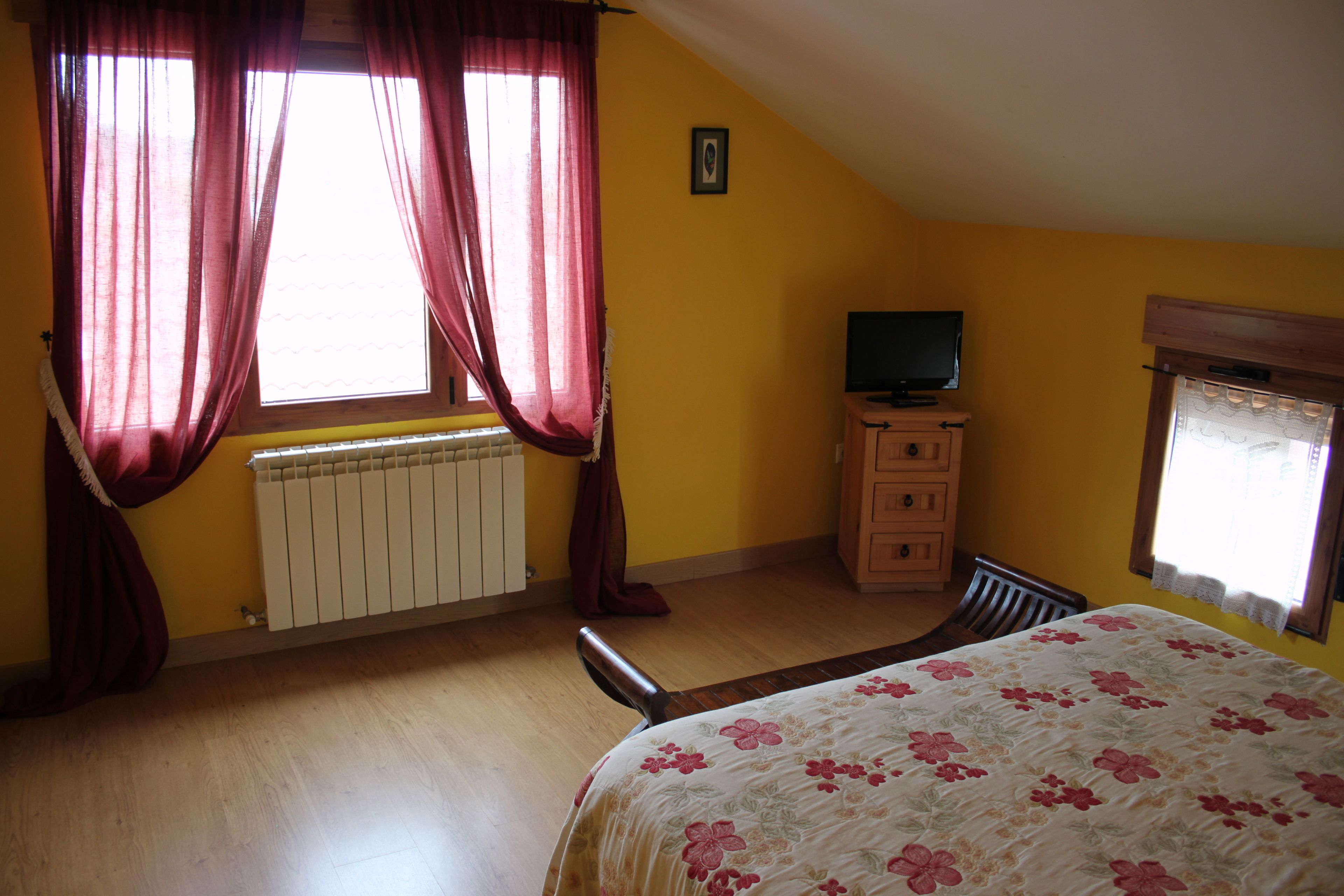 Quarto com cama, penteadeira, televisão e janela com cortinas.