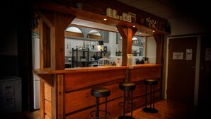 Uma área de bar com banquetas de madeira, um balcão e uma cozinha ao fundo.