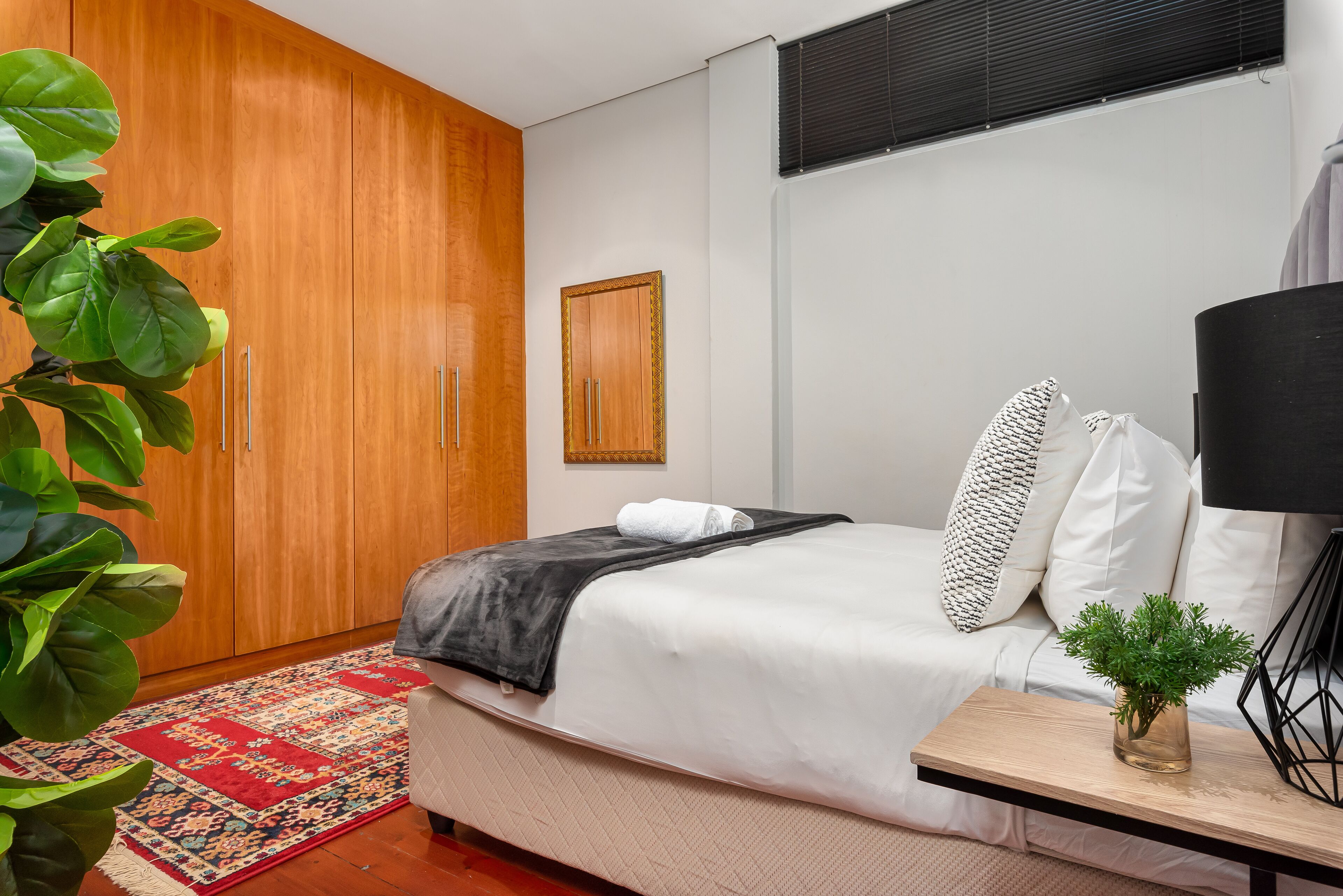 Quarto com cama, mesa de cabeceira, abajur e um vaso de plantas.