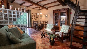 Uma sala de estar aconchegante com um sofá verde, cadeiras de madeira, uma mesa de jantar e uma escada.