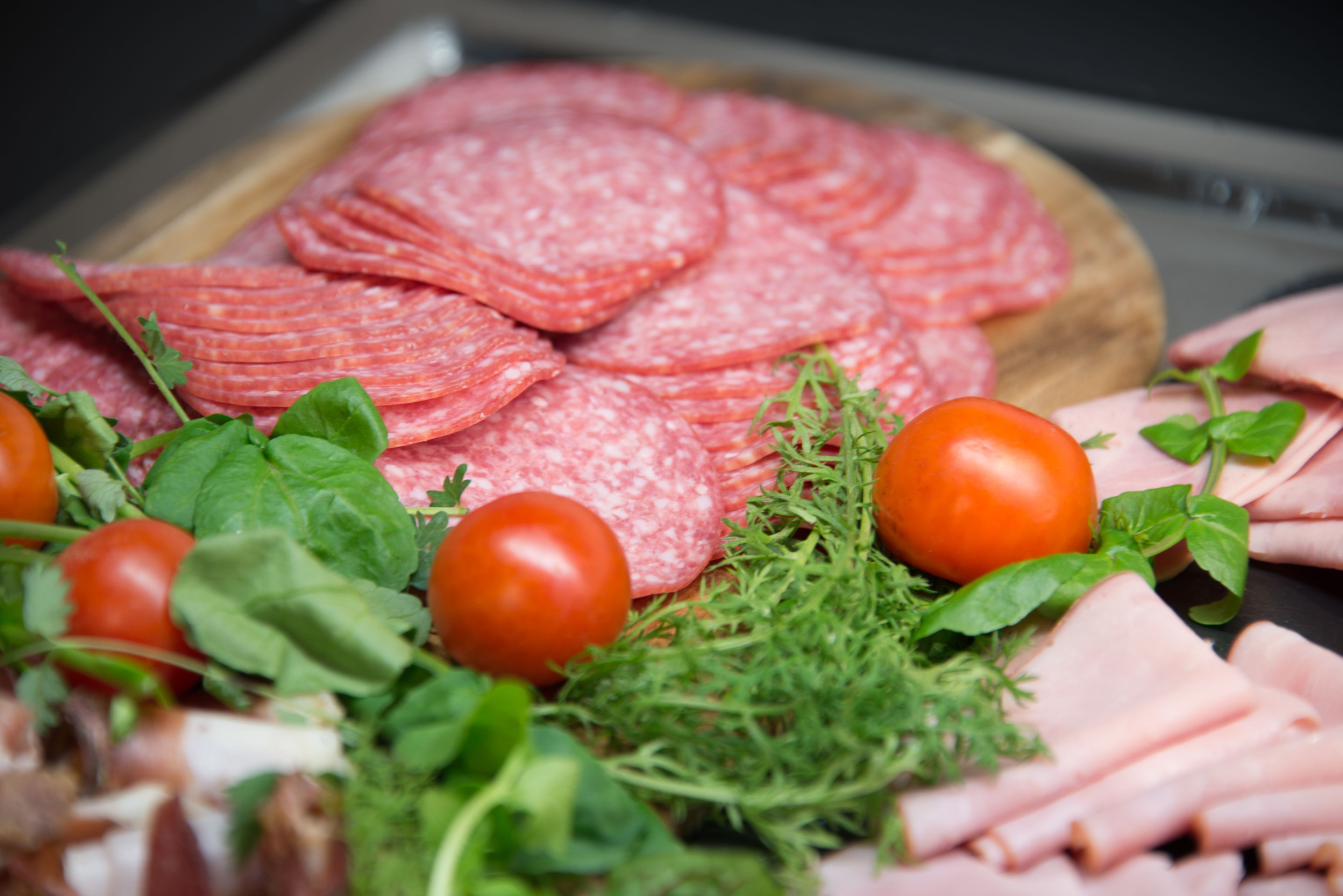 Diversos tipos de carne fatiada e legumes frescos dispostos numa tábua de madeira.