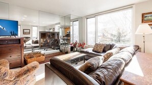 Uma sala de estar moderna com um sofá de couro, televisão e área de jantar separada por uma divisória de vidro.