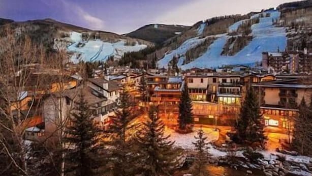 Estância de montanha com vários edifícios, encostas cobertas de neve e árvores.
