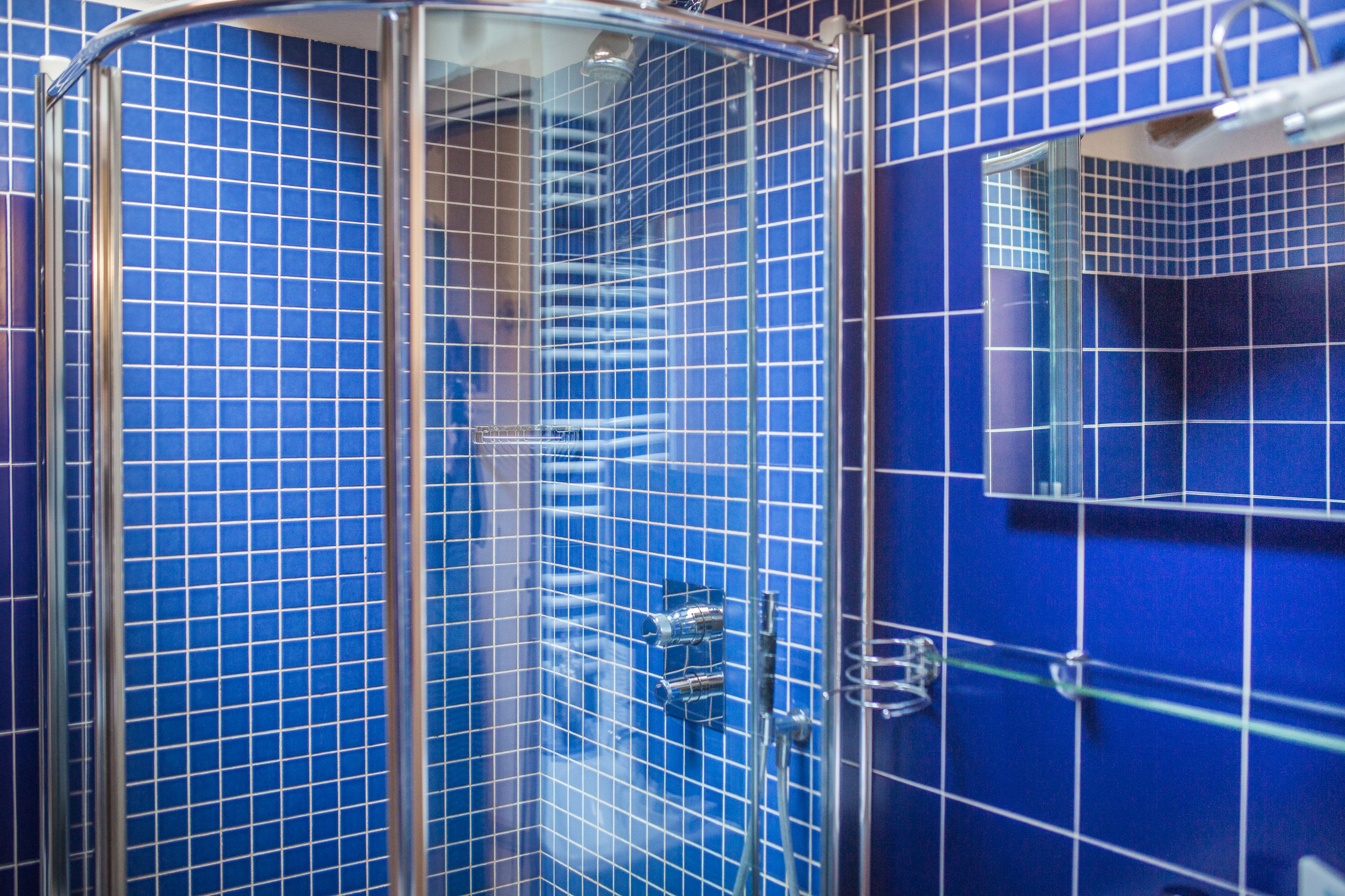 Casa de banho com paredes azulejadas em azul e cabine de duche em vidro.