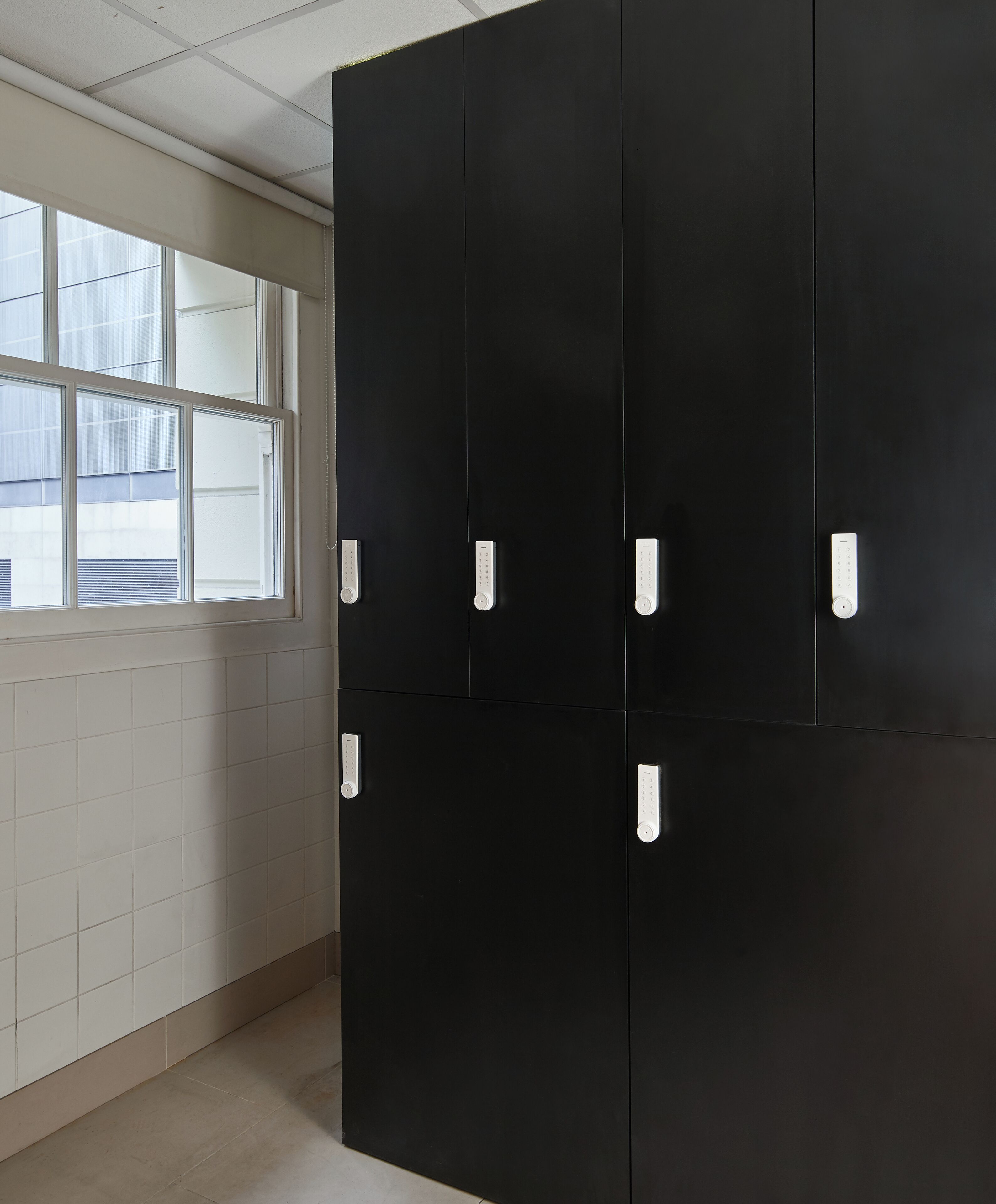 Um quarto com um guarda-roupa preto grande, uma janela com persianas e chão de azulejos.