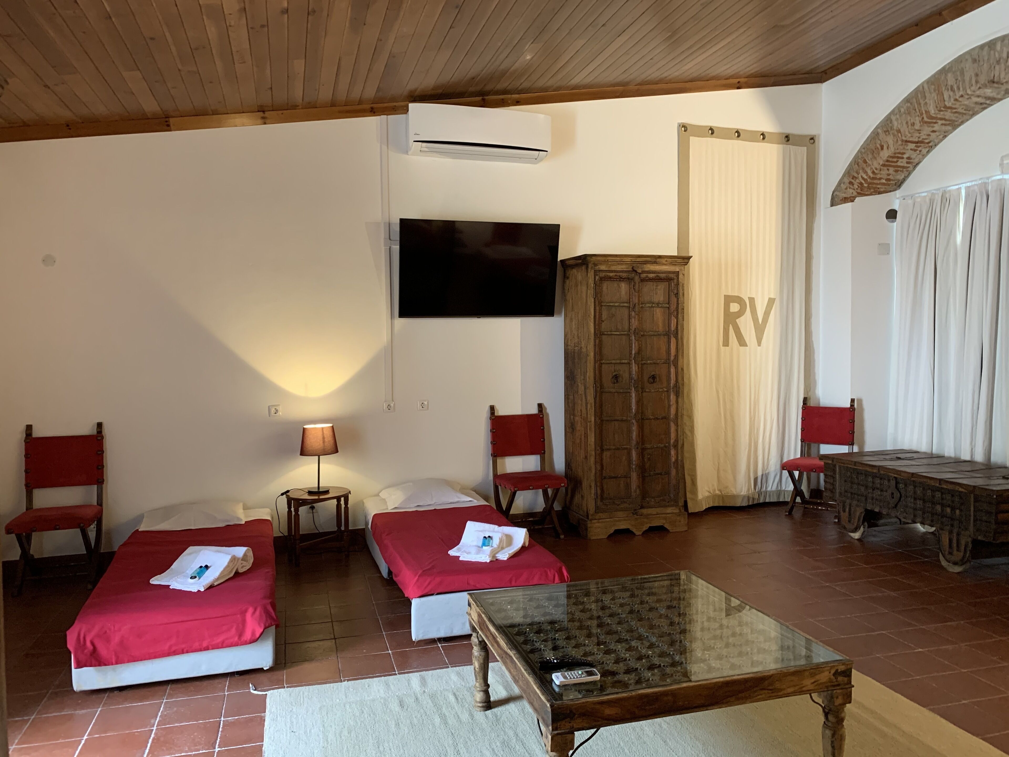 Quarto com duas camas, televisão, armário de madeira e mesa de vidro.