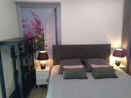 Quarto com cama, duas mesas de cabeceira, um criado-mudo, uma luminária e janela com vista para flores.