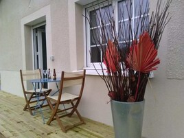 Um pátio com mesa, duas cadeiras, um vaso de planta e uma janela com vista para o céu.