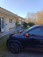Um carro preto estacionado em frente a um edifício com área de estar ao ar livre coberta e uma placa indicando vaga de estacionamento.