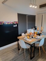 Uma sala de jantar com uma mesa posta para quatro pessoas, com uma variedade de alimentos para o café da manhã, incluindo pão, frutas e bebidas.