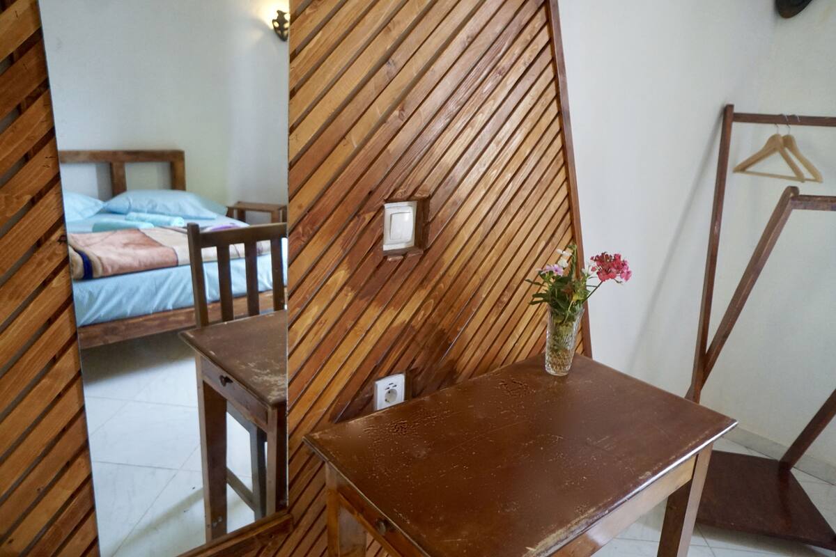 Quarto com parede de ripas de madeira, uma mesa de madeira com um vaso e uma cama com roupa de cama azul.