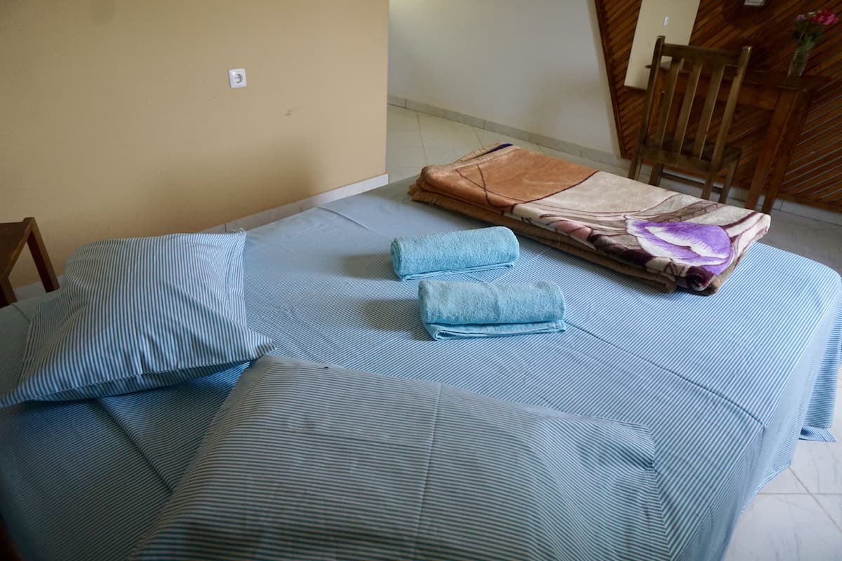 Uma cama com roupa de cama azul listrada, duas toalhas enroladas e um cobertor floral.