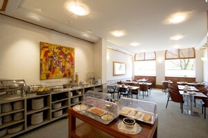 Espaço de refeições com balcões de buffet, mesas e cadeiras.