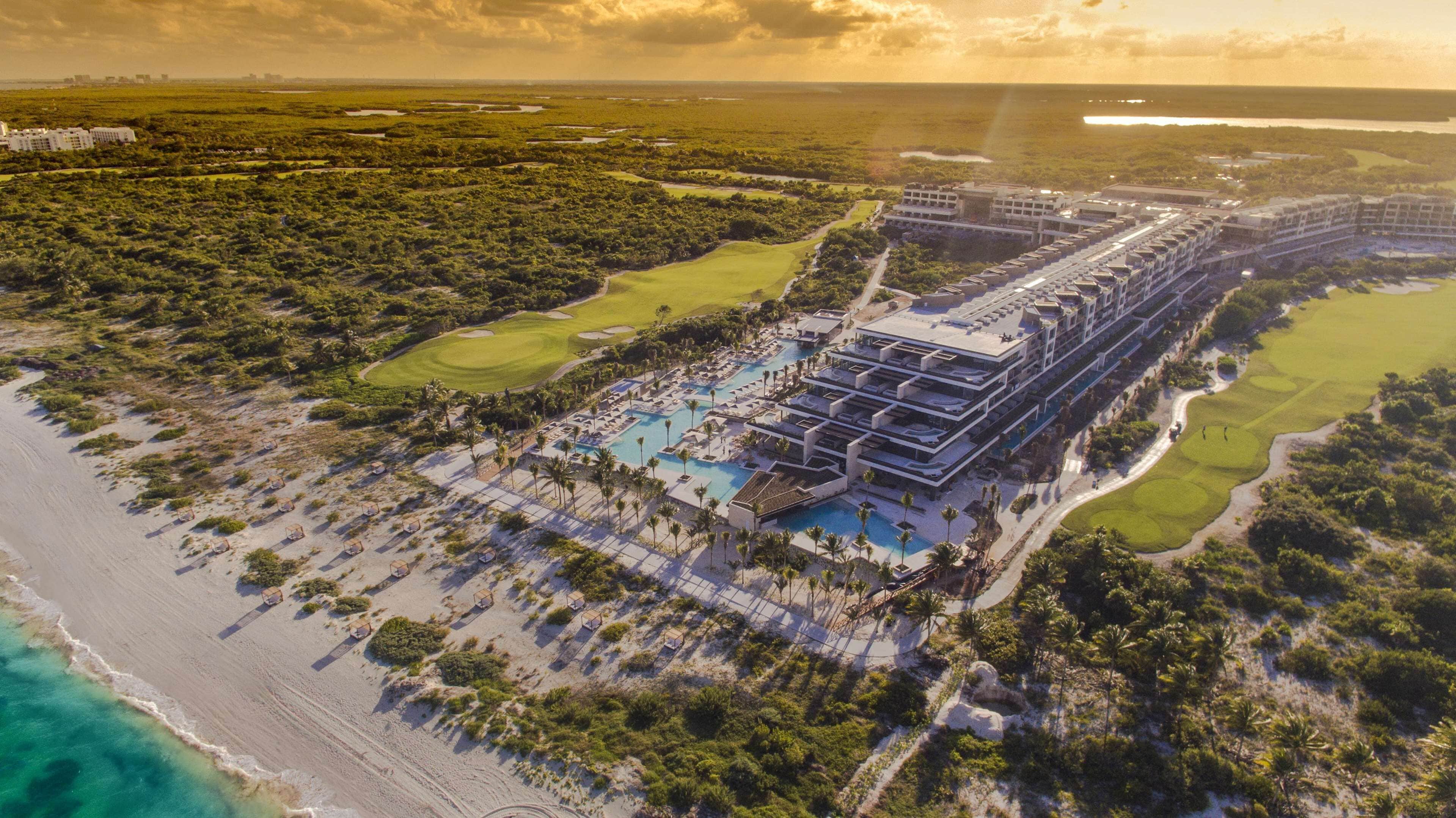 Vista aérea de um resort com várias piscinas, campo de golfe e acesso à praia.