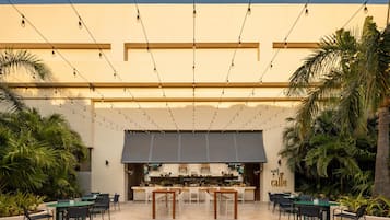 Uma área de refeições ao ar livre com mesas, cadeiras, balcão de bar e luzes de corda.