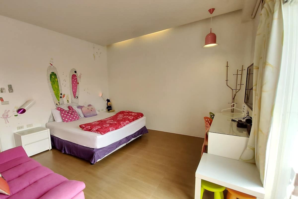 Um quarto com uma cama, uma escrivaninha, uma cadeira e um sofá rosa.
