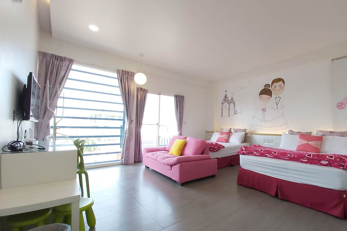 Quarto moderno com um sofá rosa, uma cama com colcha vermelha e branca, uma TV de tela plana e uma janela grande com cortinas.