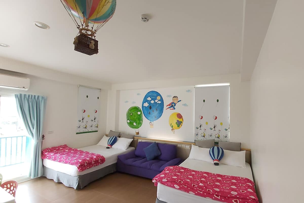 Quarto com duas camas, um sofá roxo e uma parede com desenhos infantis.